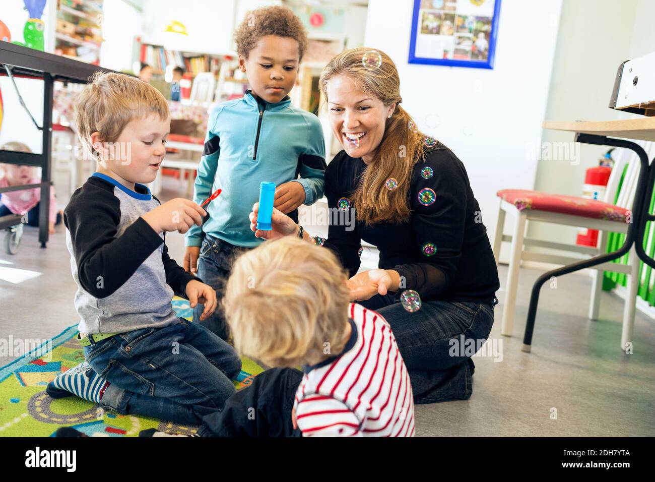 Happy teacher and children playing with bubbles in kindergarten Stock ...