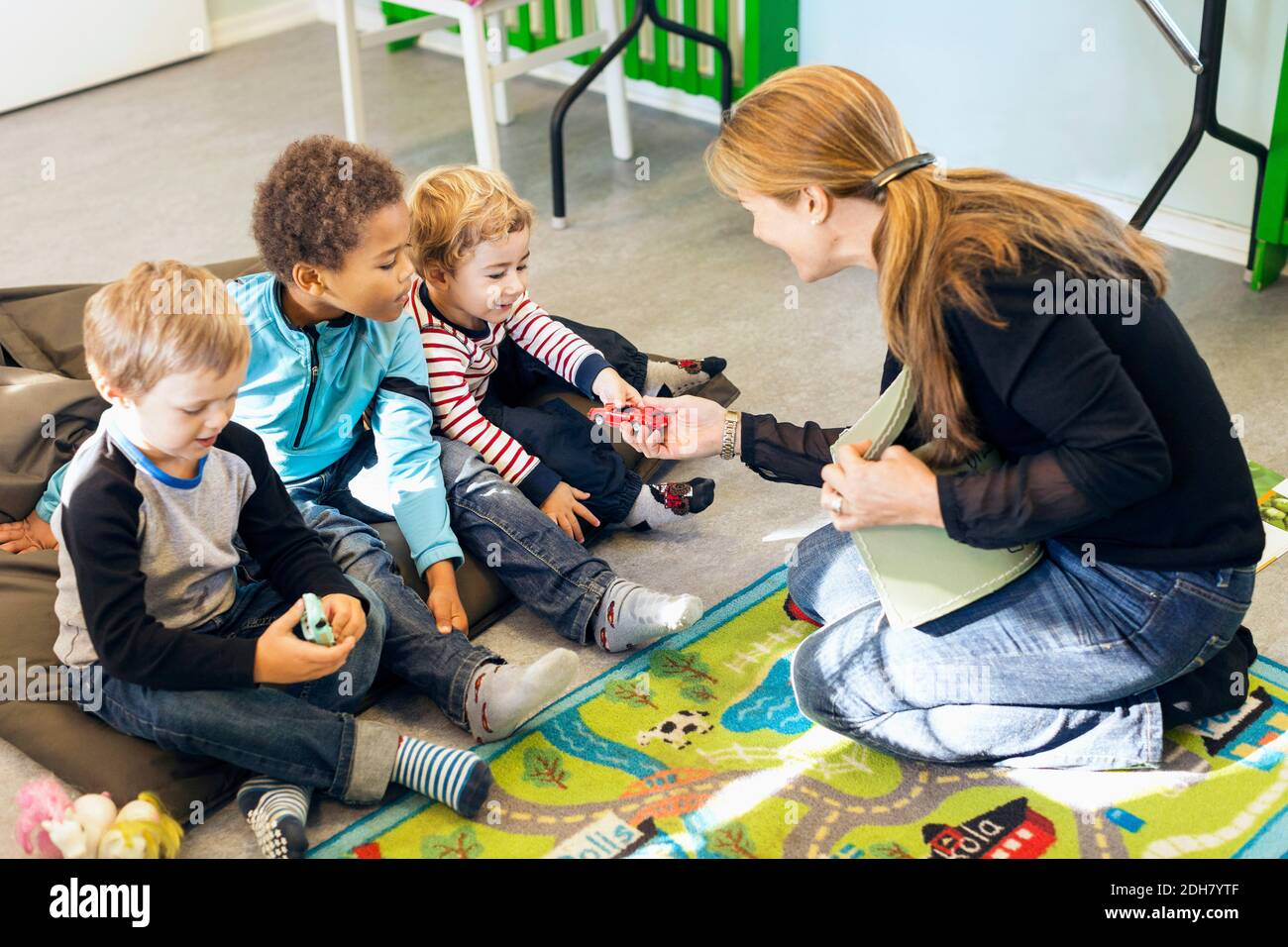 Full length of teacher giving toys to children Stock Photo - Alamy