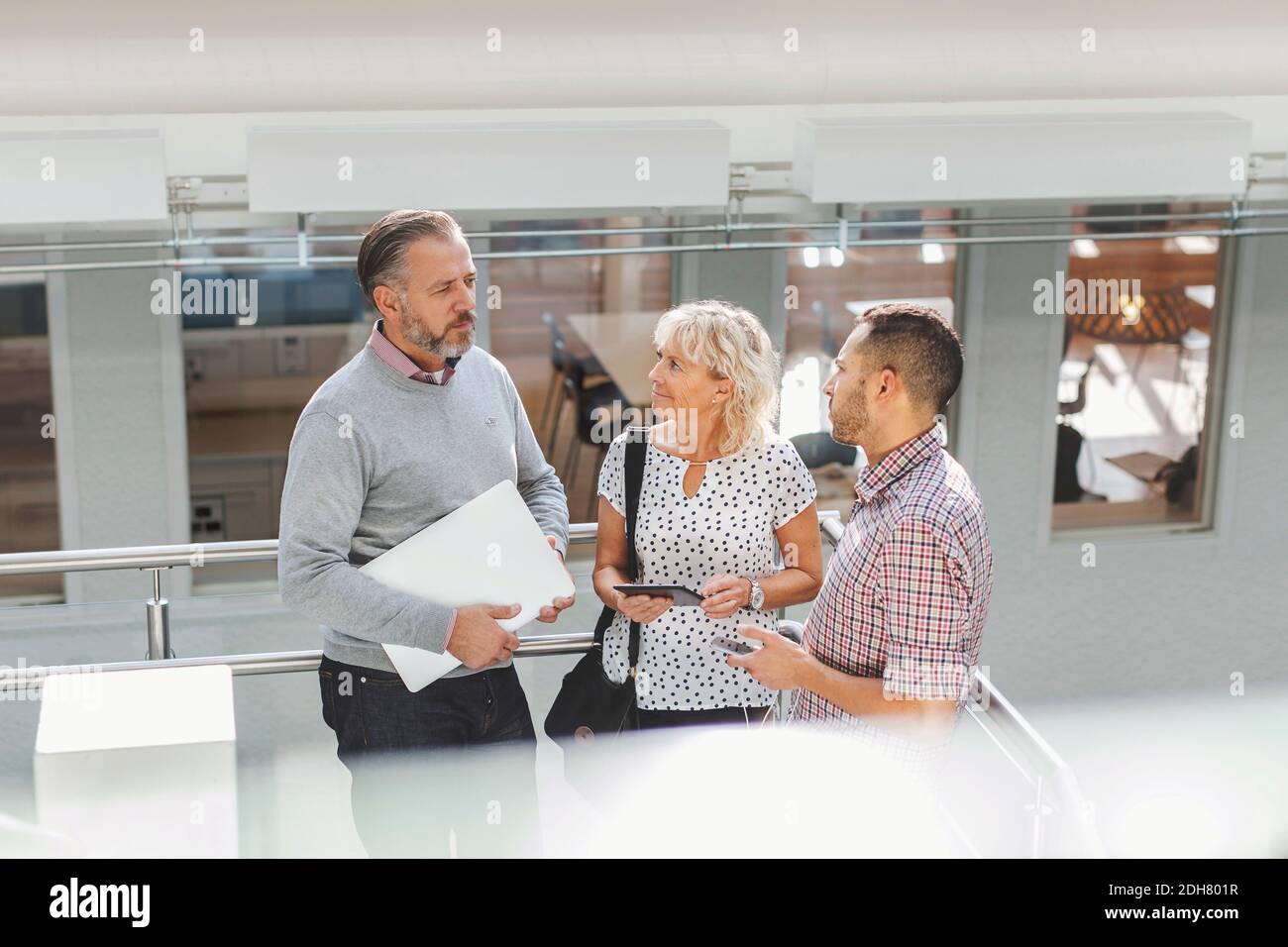 Businesspeople discussing by railing in modern office Stock Photo - Alamy