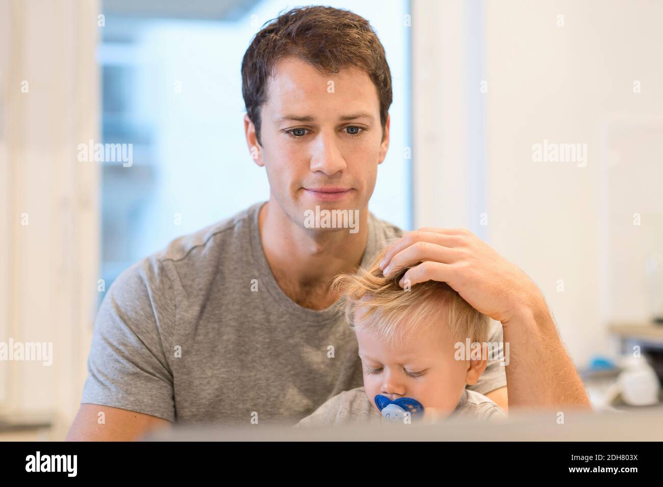 Baby boy sitting with father working on laptop in house Stock Photo - Alamy