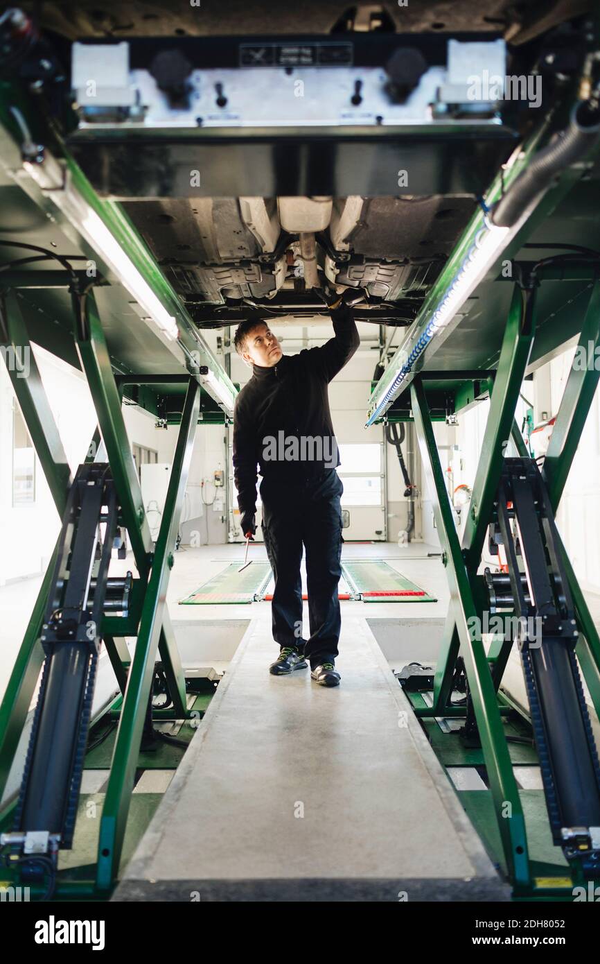 Full length of male mechanic examining car on hydraulic lift in auto ...