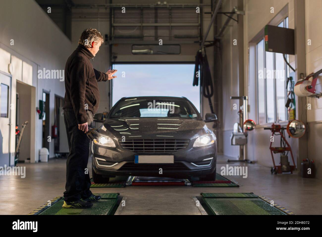 Full length of mechanic showing stop gesture towards car on hydraulic ...