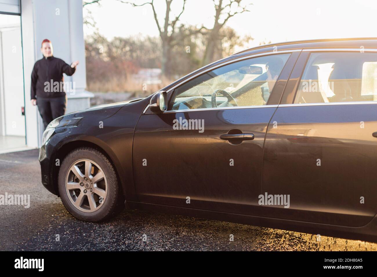 Man driving car while female mechanic guiding him outside auto repair ...