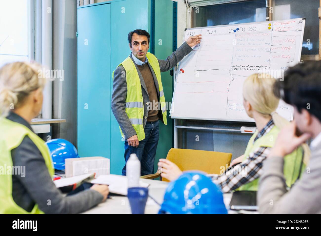 Mature male worker explaining plan on whiteboard to colleagues in ...