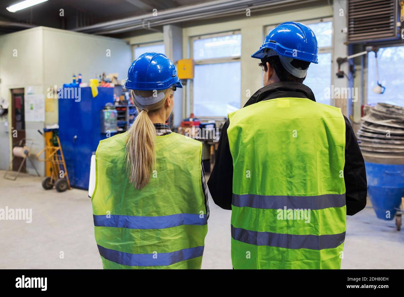 Rear view of male and female workers in protective workwear at factory ...