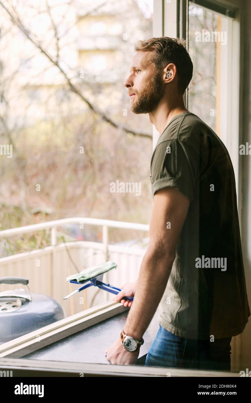 Side view of thoughtful man looking through window Stock Photo - Alamy