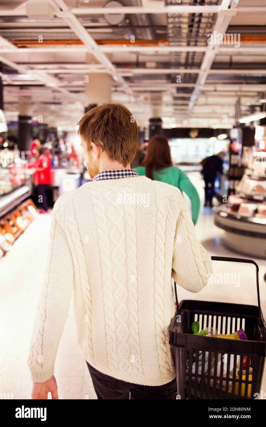 Rear view of man carrying basket while walking at supermarket Stock ...