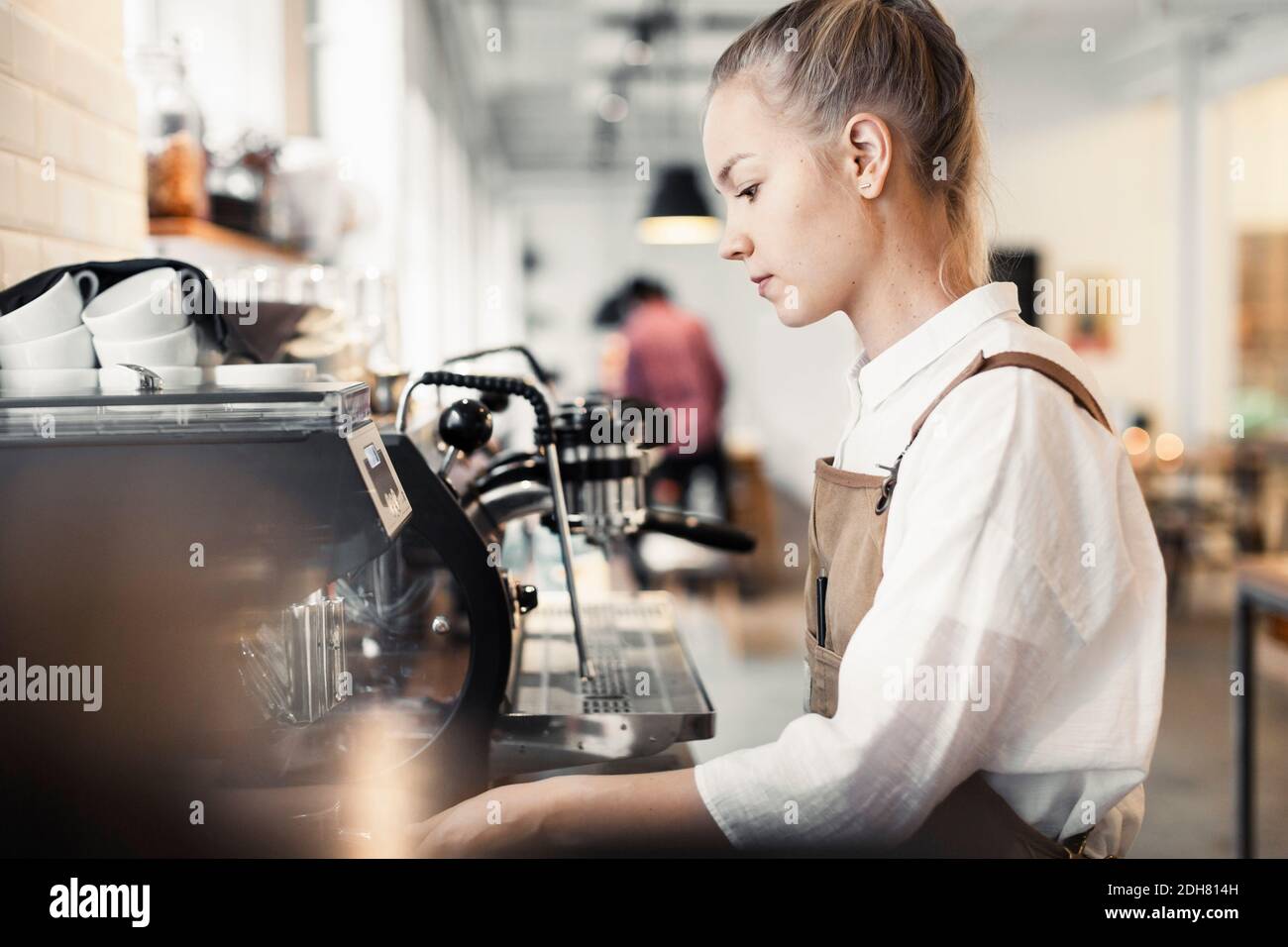 Side view of young female barista using espresso maker at cafe Stock ...
