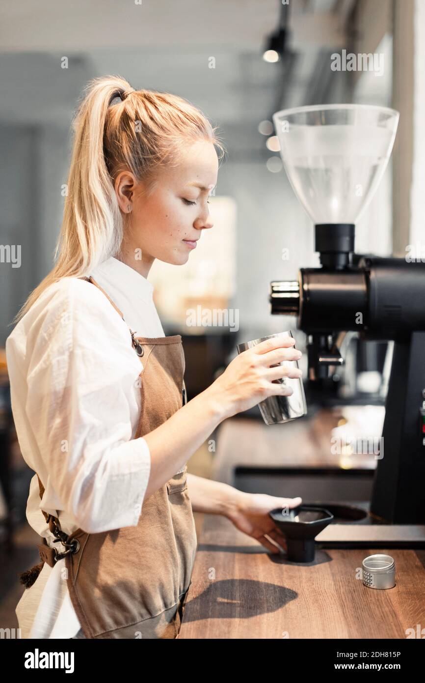 Side view of female barista holding container by coffee maker at ...