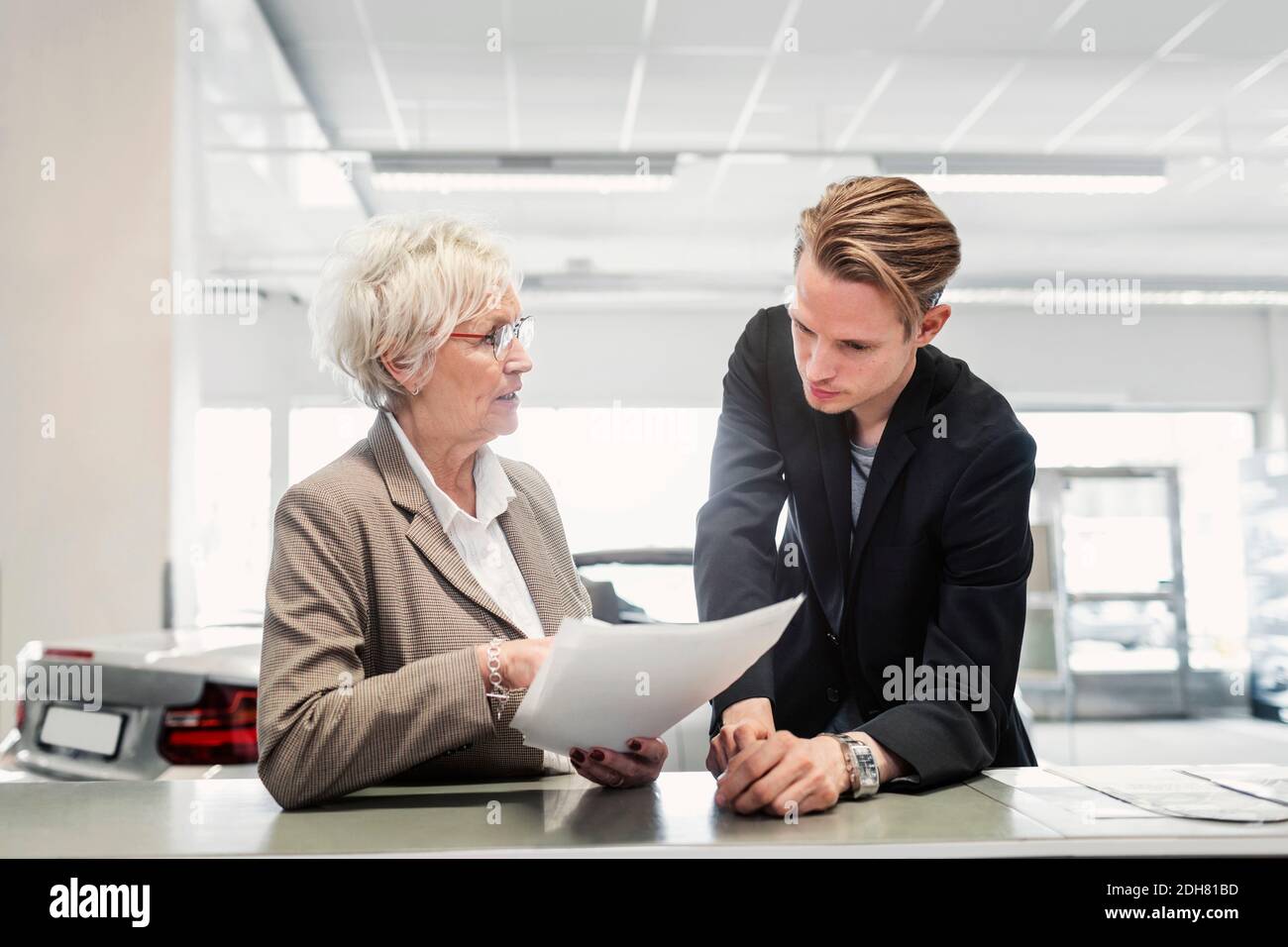 Two sales colleagues discussing documents at car dealership Stock Photo ...