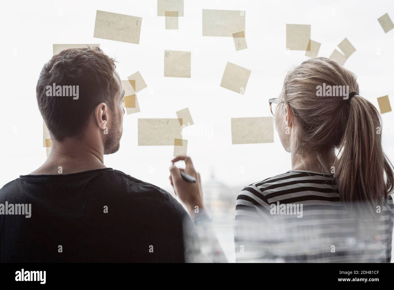 Rear view of business colleagues reading adhesive notes stuck to glass ...
