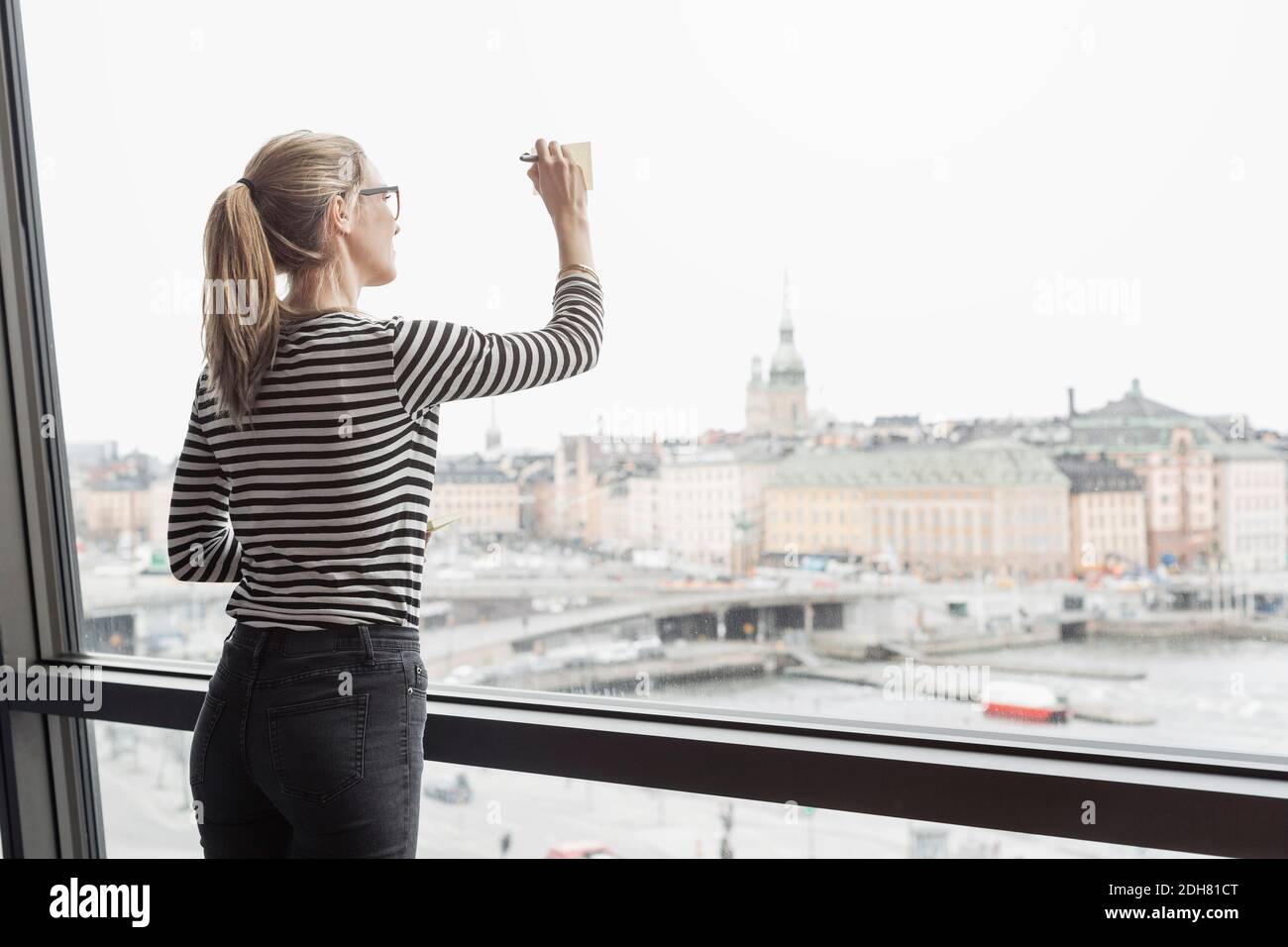 Rear view of businesswoman writing on adhesive note stuck to glass ...