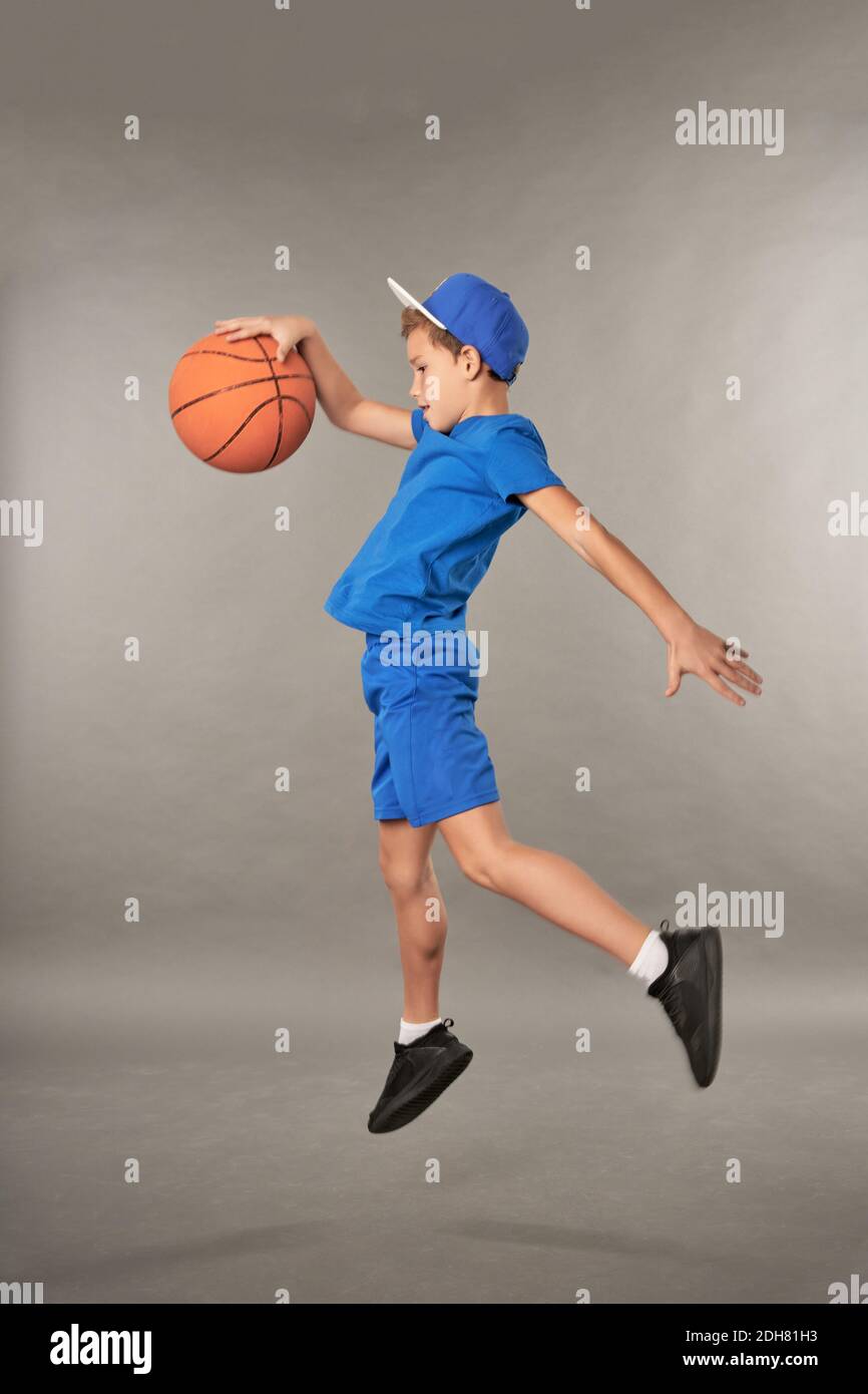 Cute male child in sportswear jumping in the air and holding basketball ...