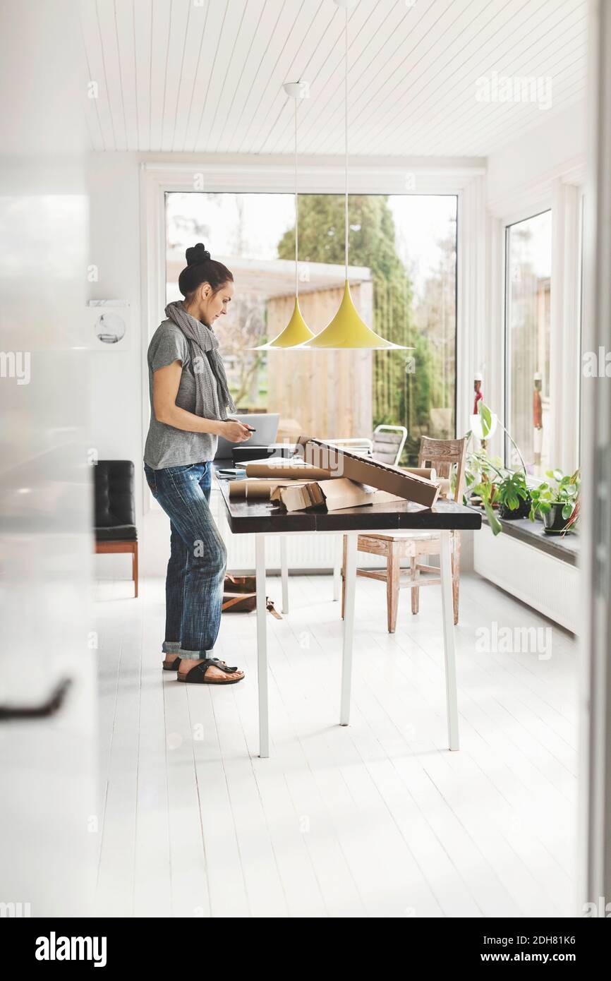 Full length side view of female architect working at table in home ...