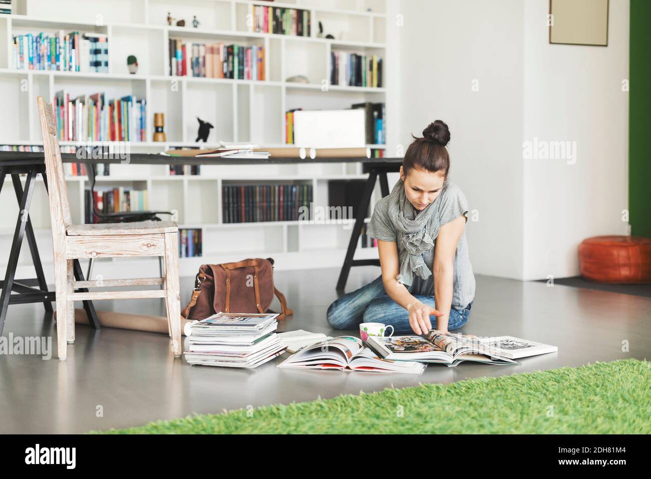 Female architect reading magazine on floor at home office Stock Photo ...