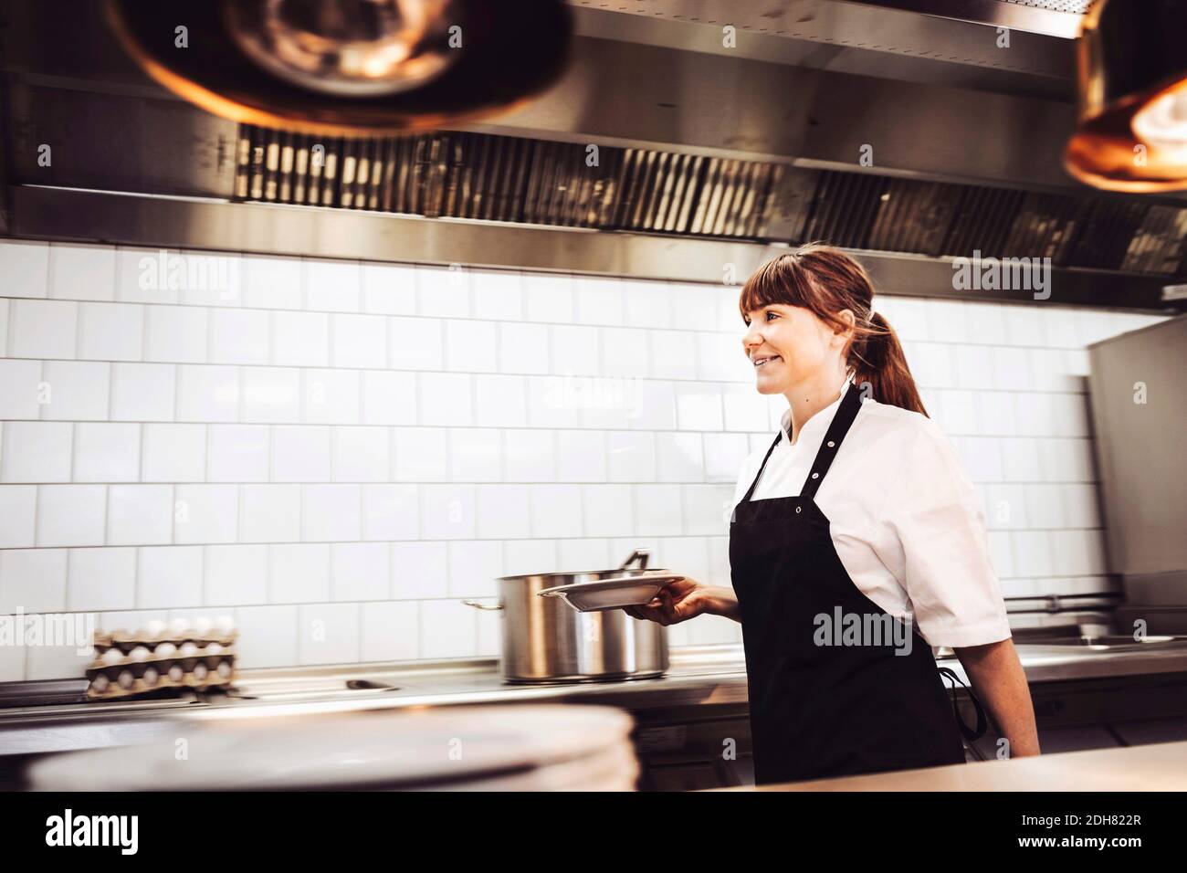 Female chef holding plate white walking in commercial kitchen Stock ...