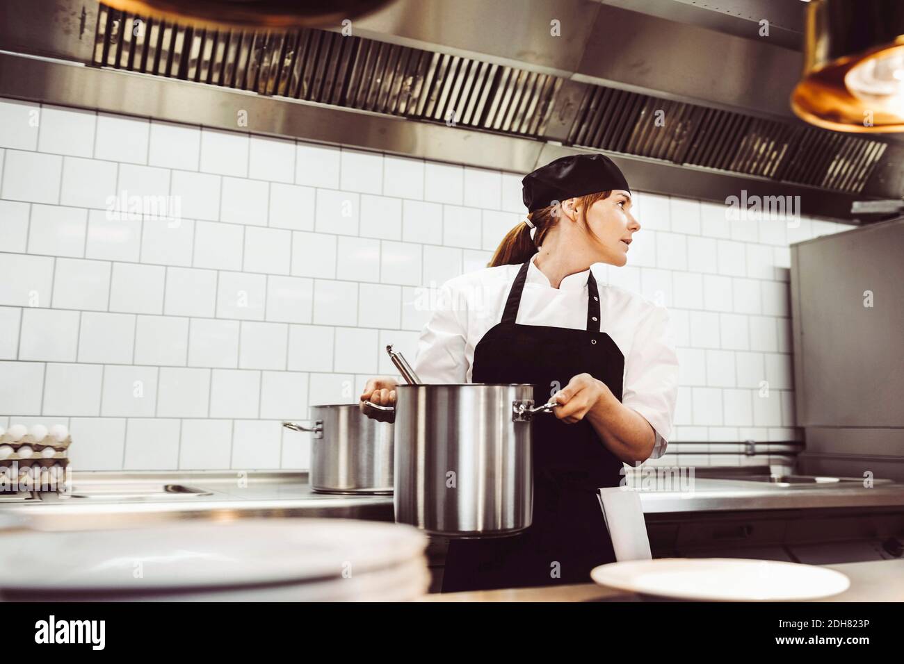 Female chef looking away while holding container in commercial kitchen ...