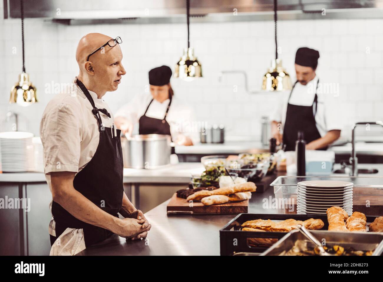 Manlig kock pratar i storkök med två kockar i bakgrunden Stock Photo ...