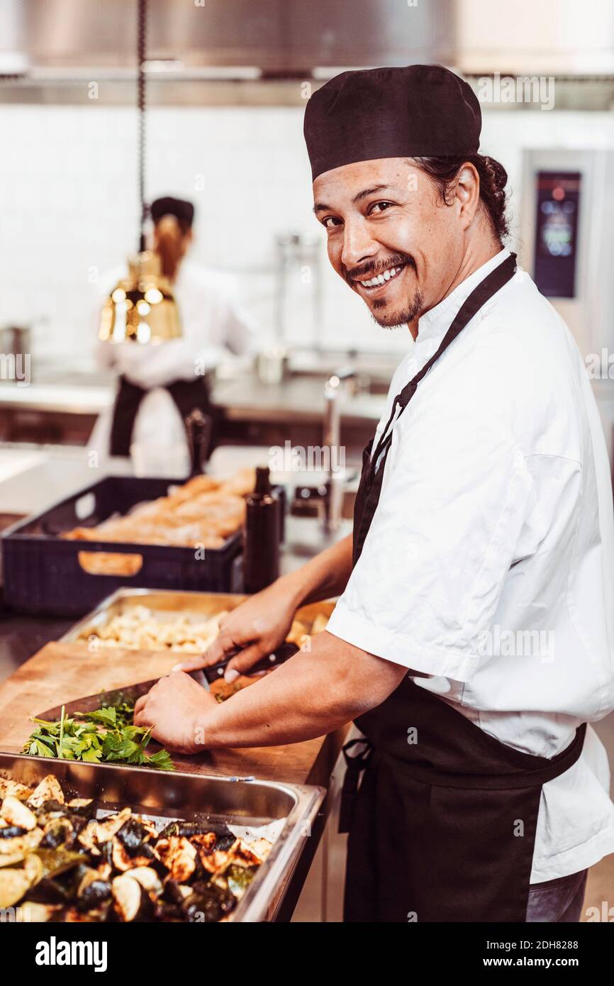 Side view portrait of happy male chef cutting leafy vegetables at ...