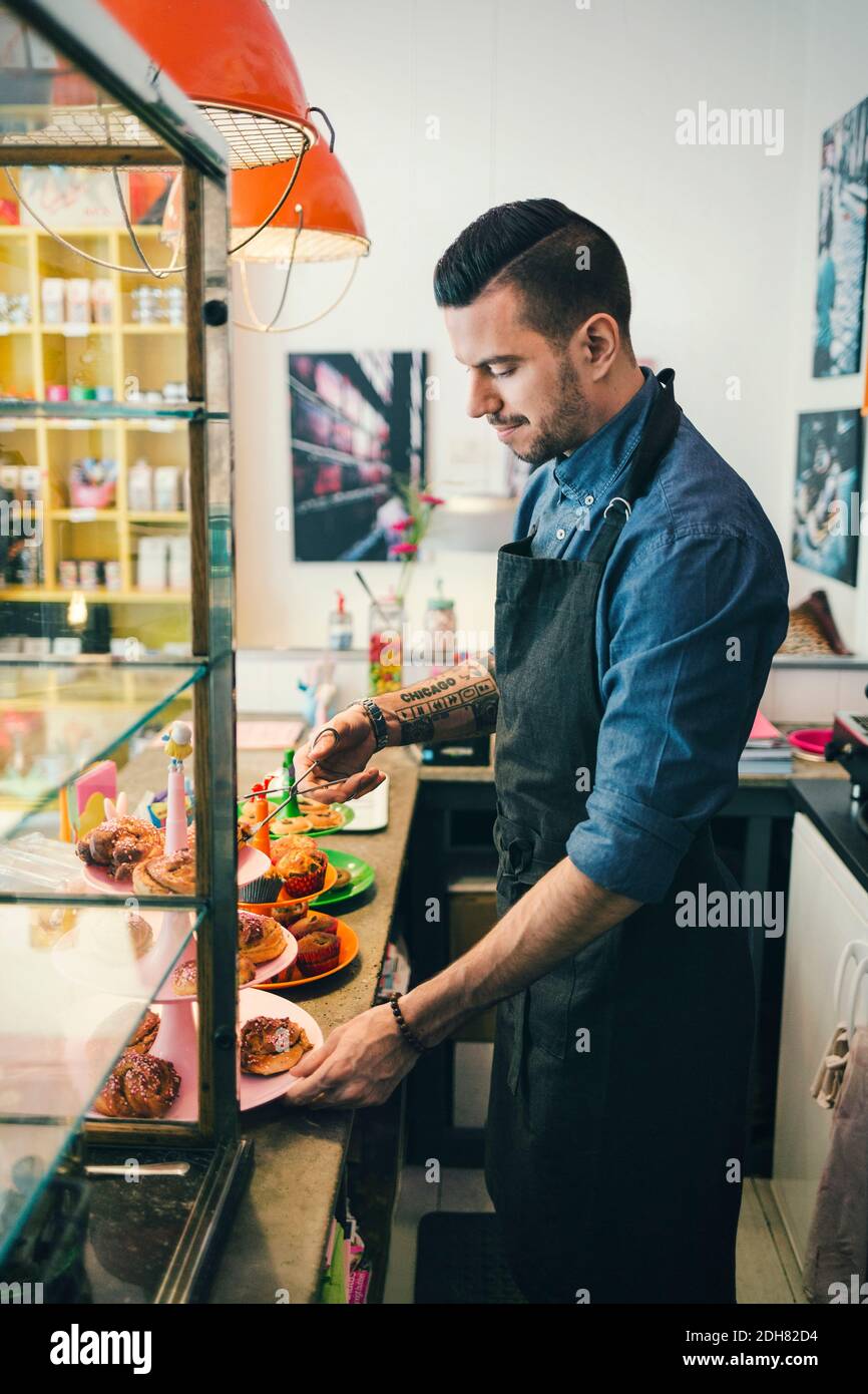 Side view of barista with pastries at cafe counter Stock Photo - Alamy