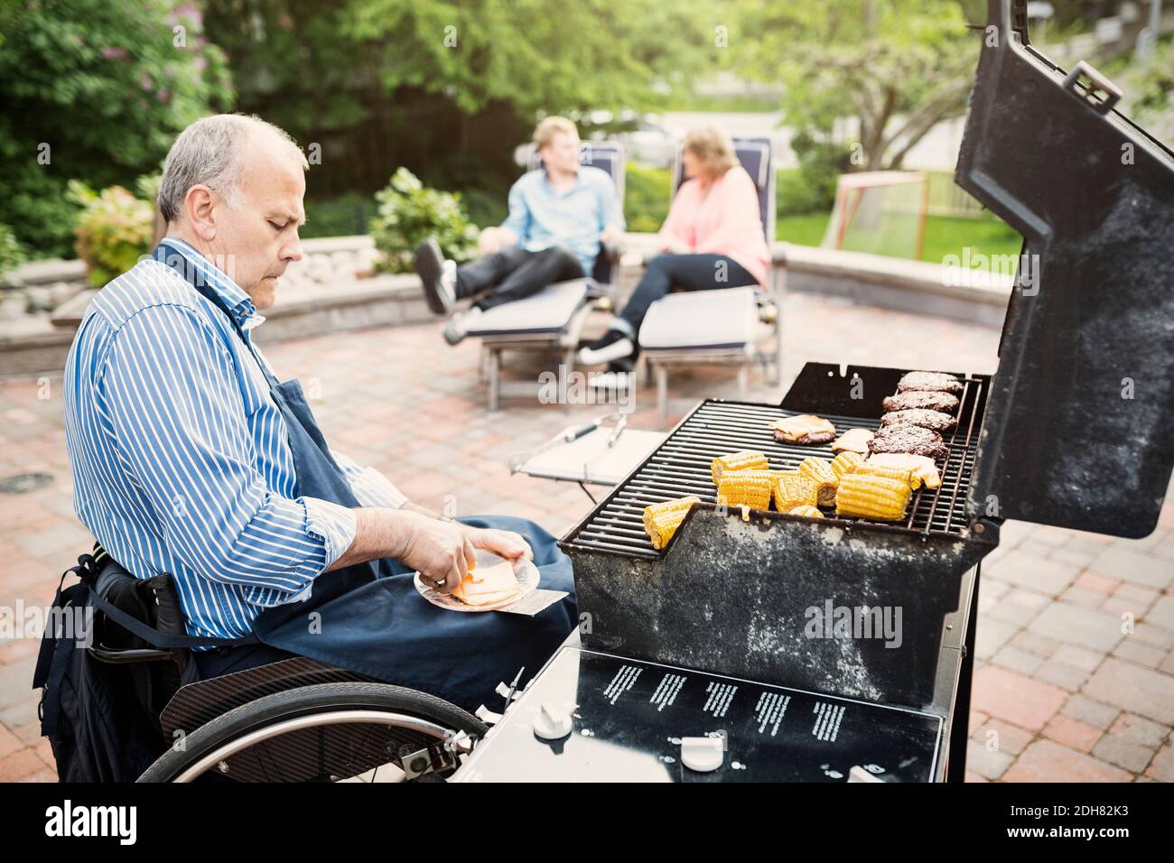 Disabled man barbecuing while family sitting in background at yard ...
