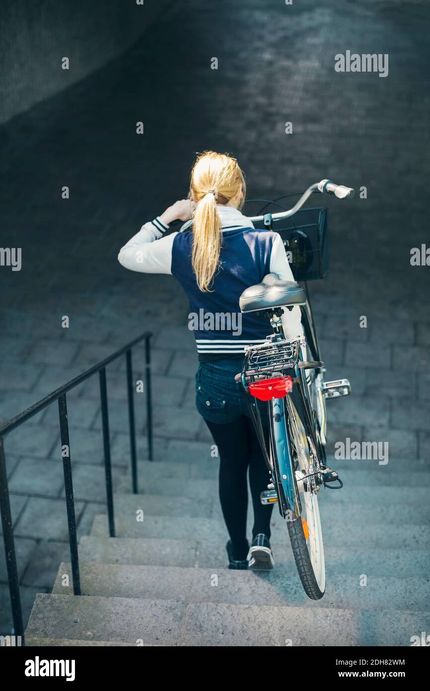 Rear view of businesswoman carrying bicycle while moving down steps ...