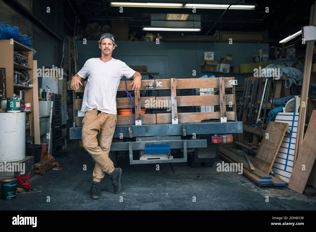 Full length portrait of carpenter leaning on pick-up truck at workshop ...