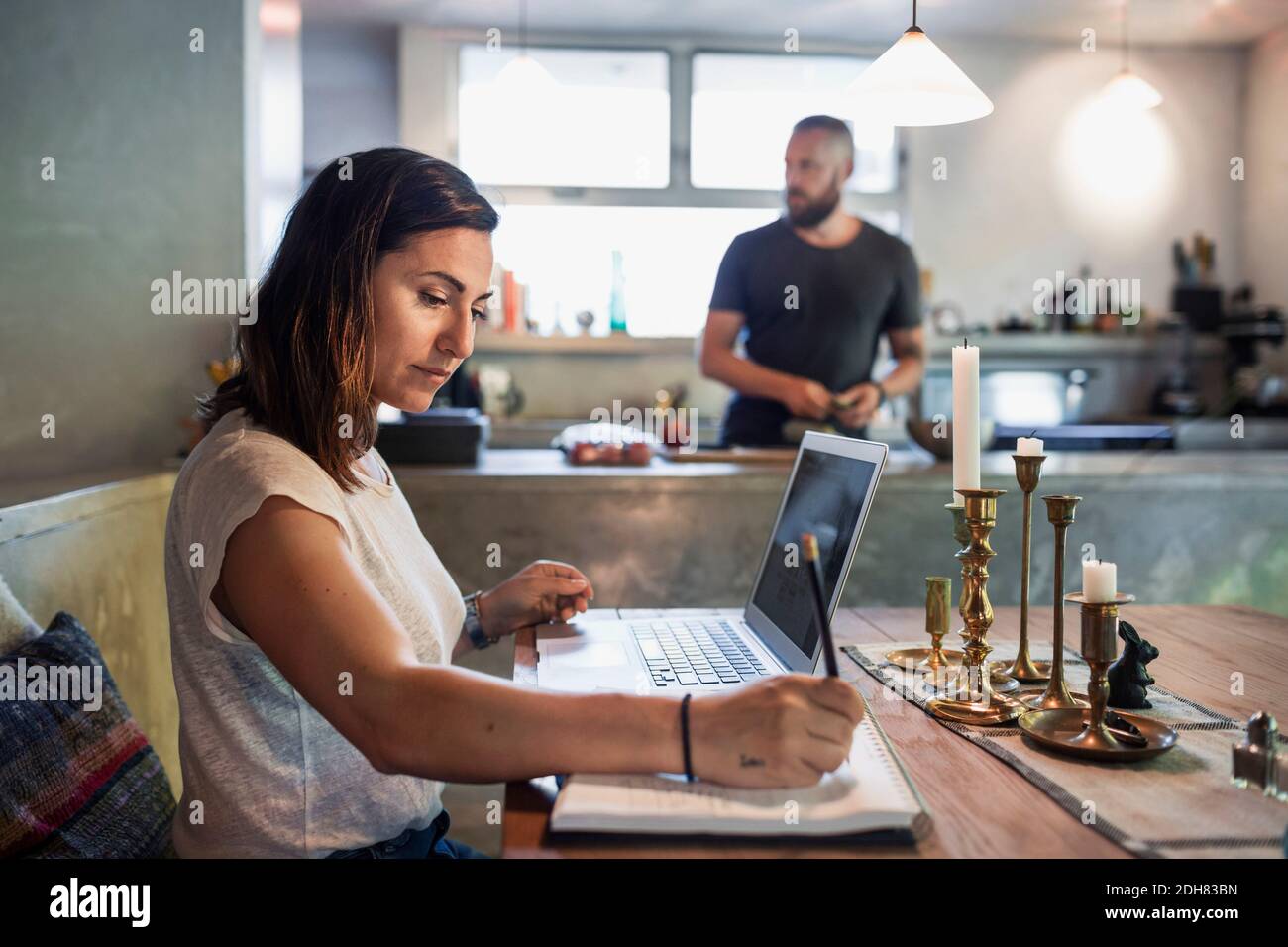 Side view of woman working at dining table while man standing in ...