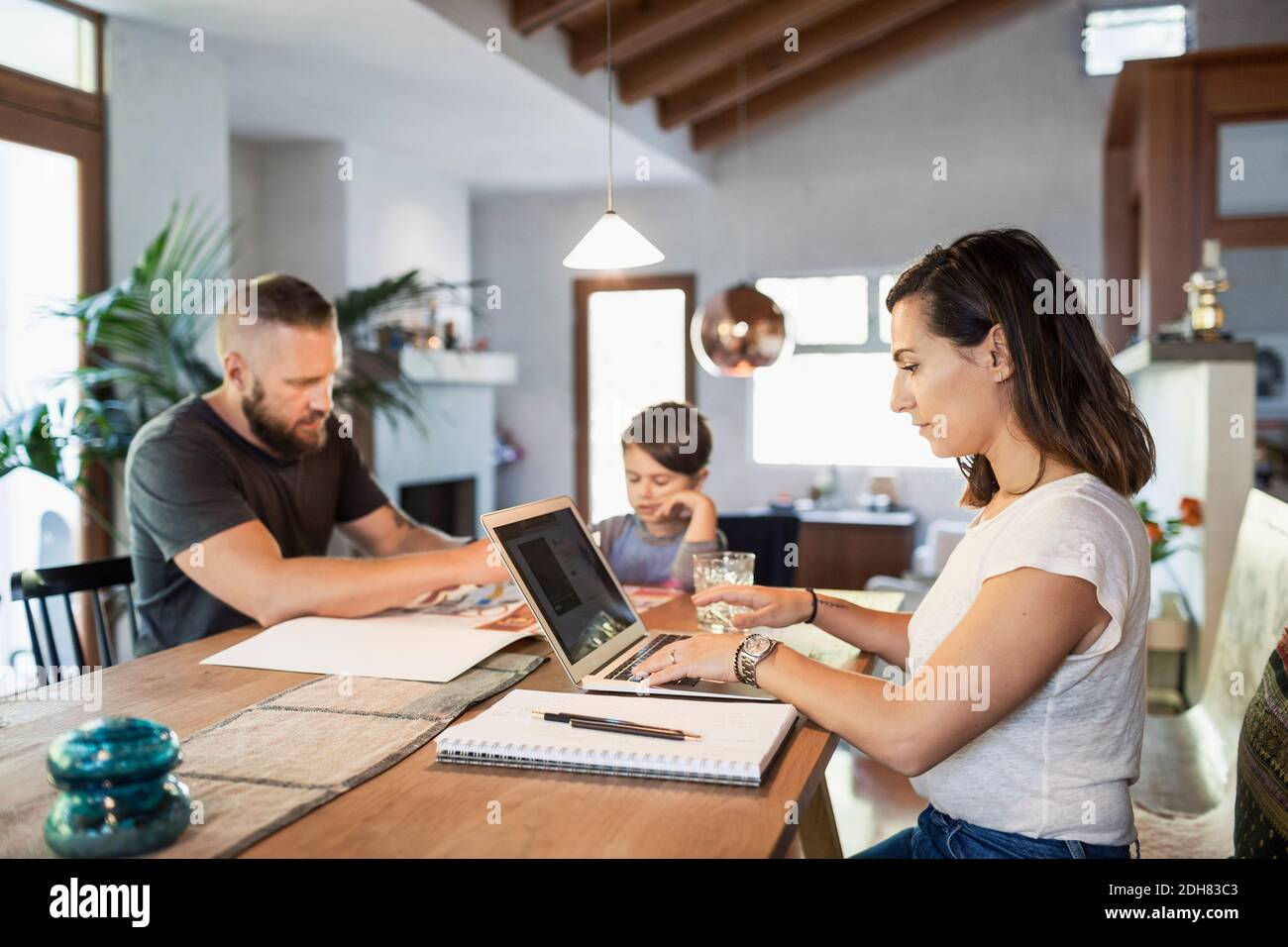 Woman working on laptop at dining table with family in background Stock ...