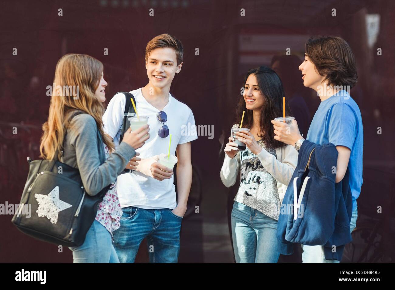 Happy teenage friends talking while holding drinks outdoors Stock Photo ...
