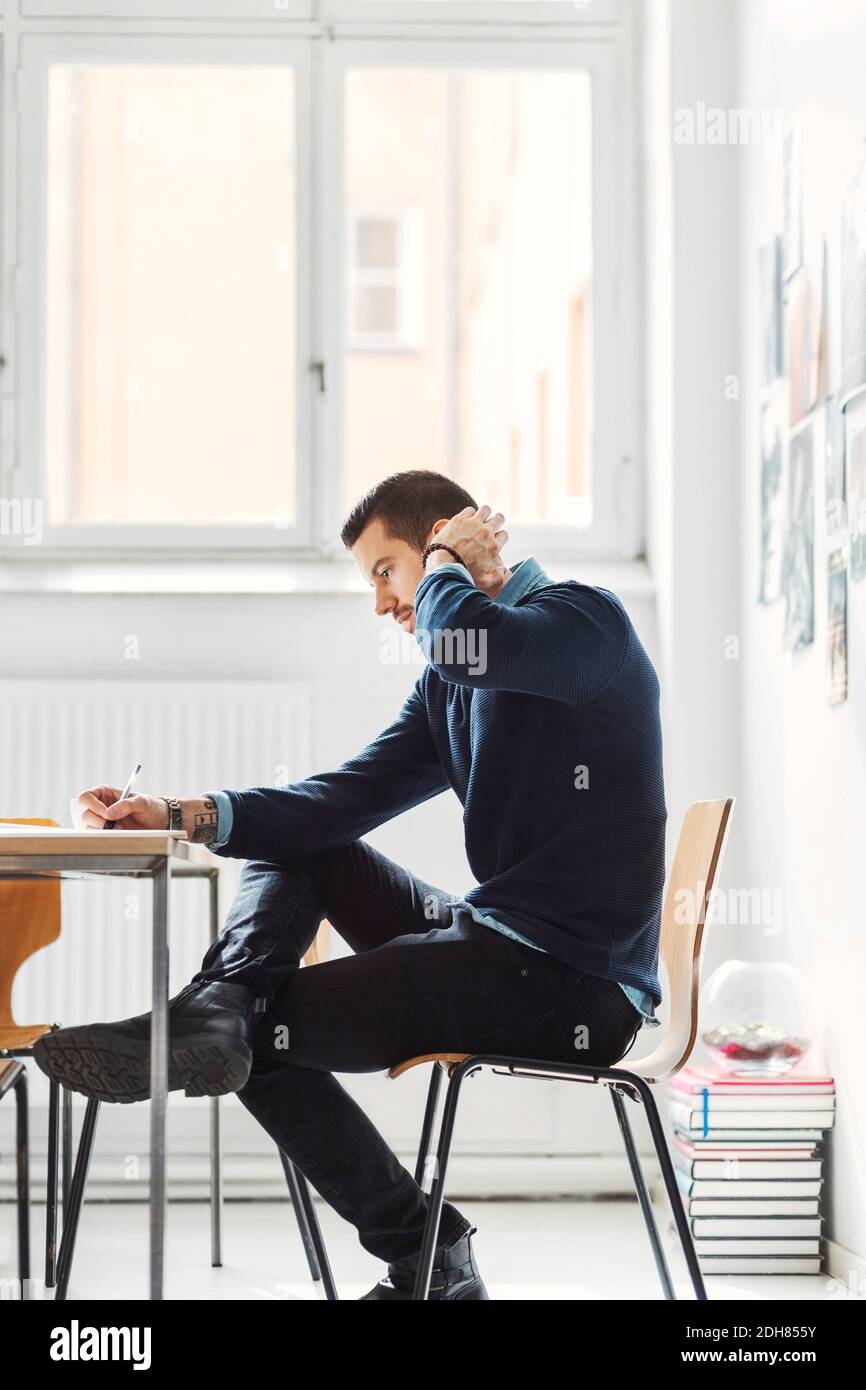 Side view of mid adult businessman writing in book at office desk Stock ...