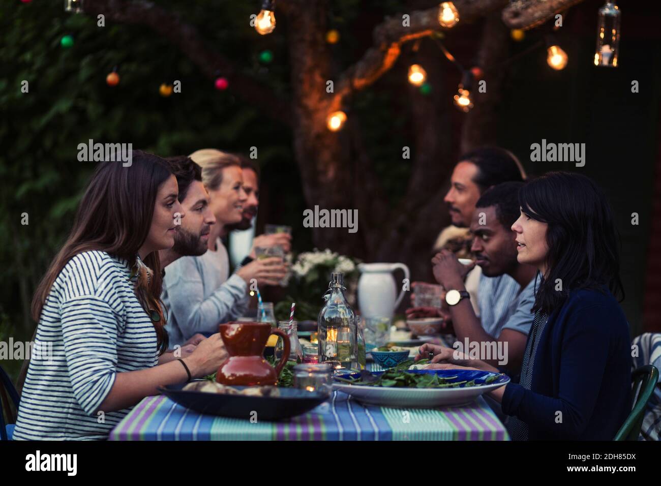 Side view of happy multi-ethnic friends having dinner at table in yard ...