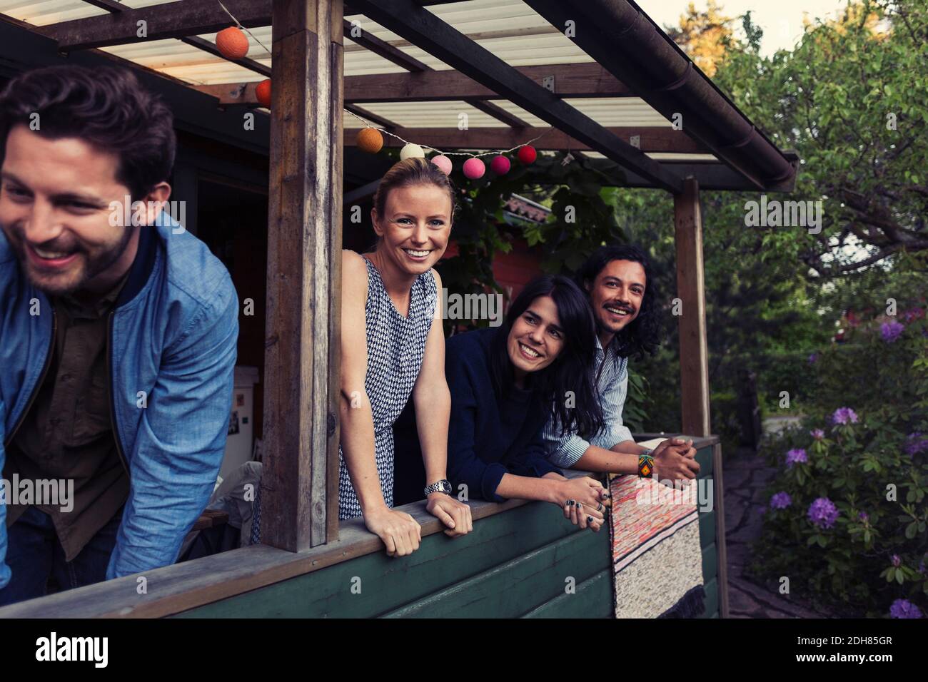 Portrait of happy young woman standing with friends on porch at log ...