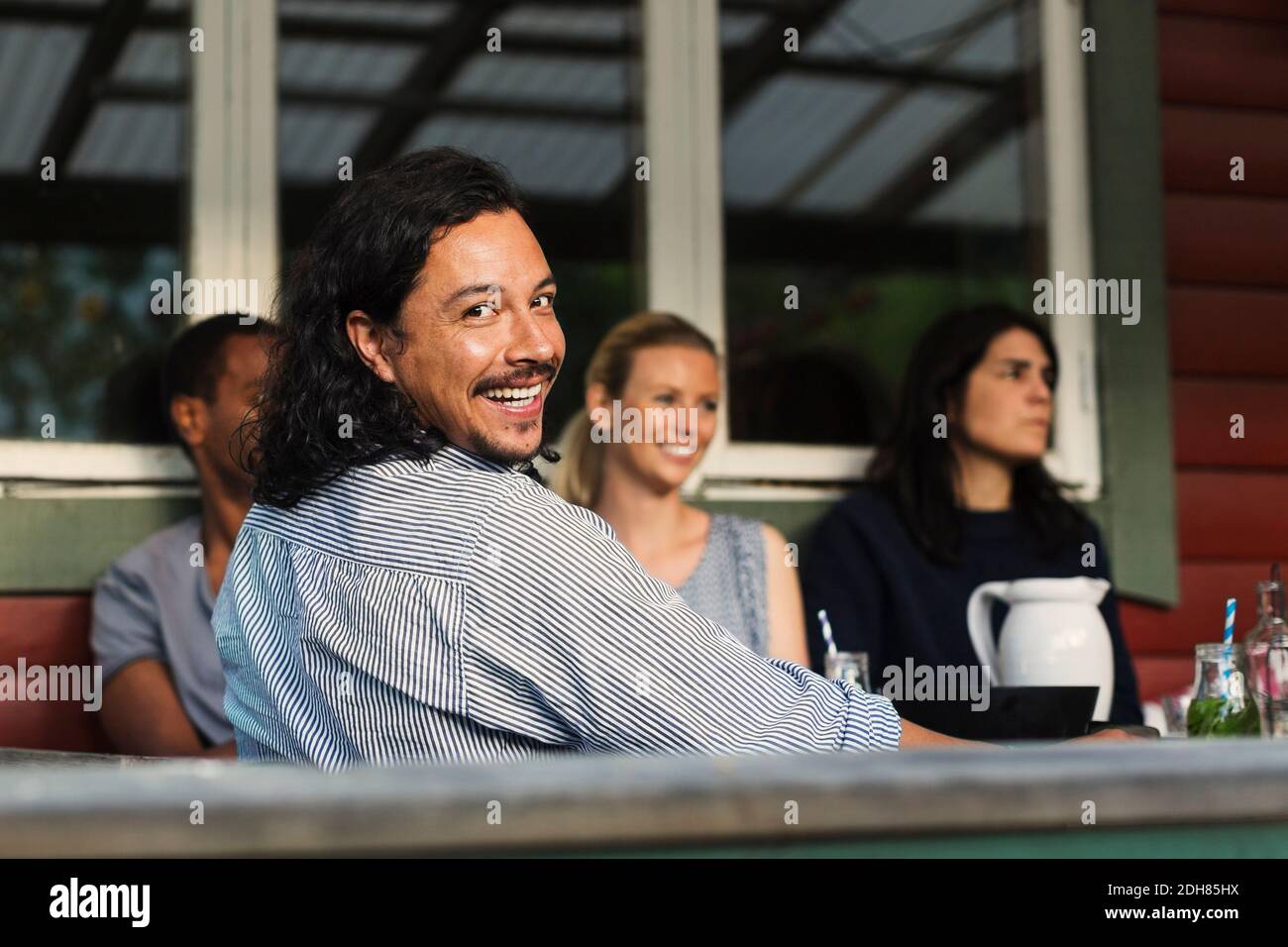 Rear view portrait of happy man sitting with friends at log cabin Stock ...