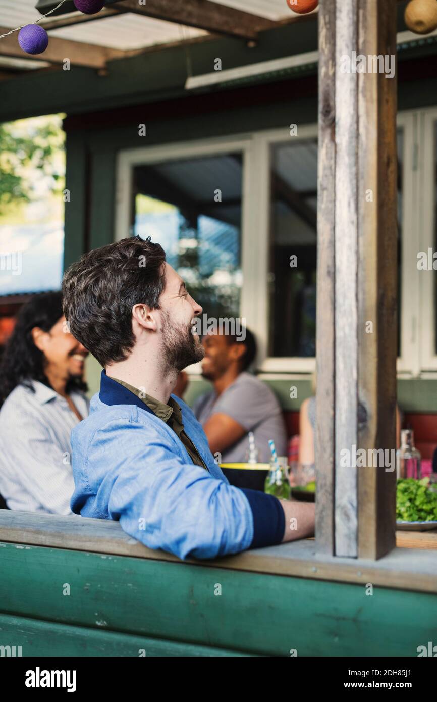 Side view of happy man sitting at porch while enjoying summer party ...