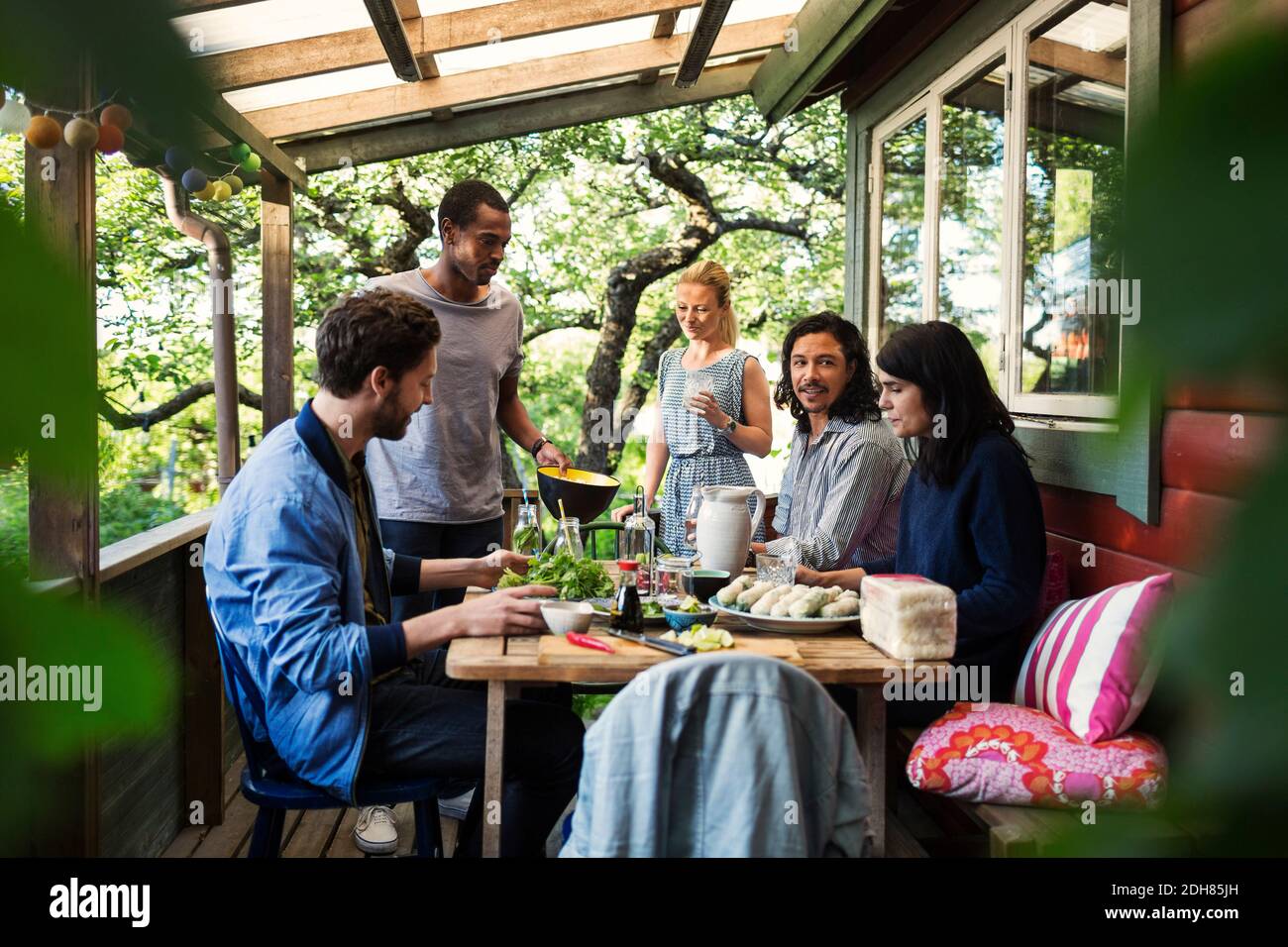 Multi-ethnic friends having food on porch at log cabin during summer ...
