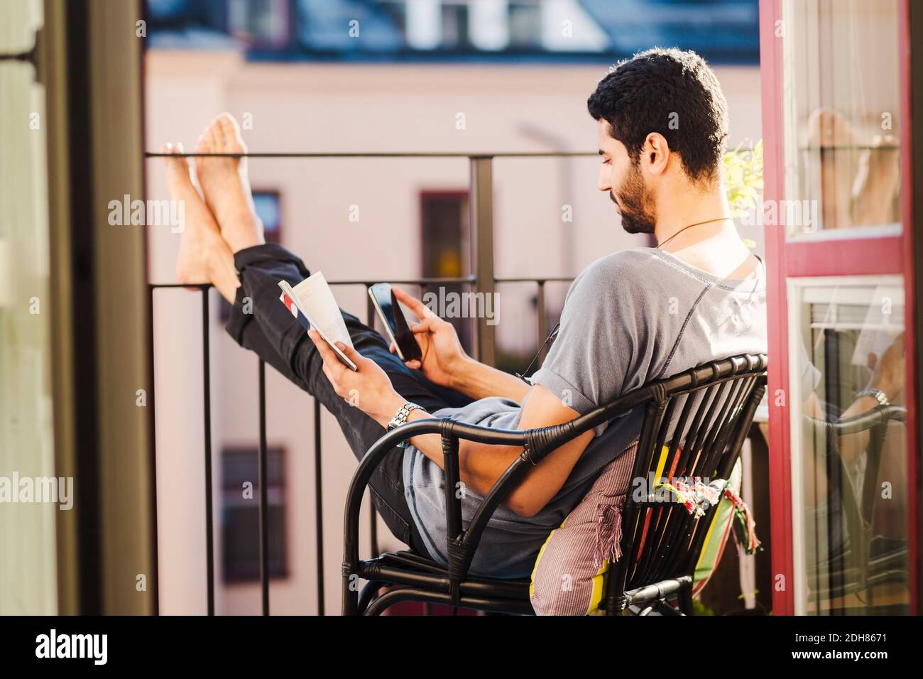 Side view of man using smart phone while holding guidebook at balcony ...