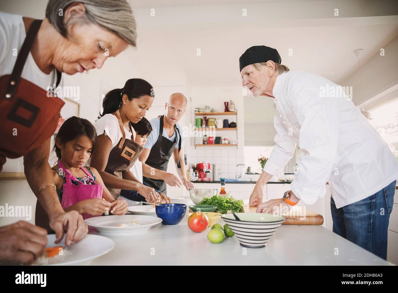 Senior man guiding family in preparing Asian food at kitchen Stock ...