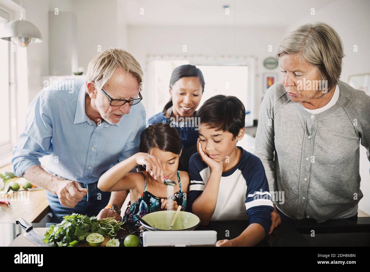 Family looking at girl preparing food at kitchen counter Stock Photo ...