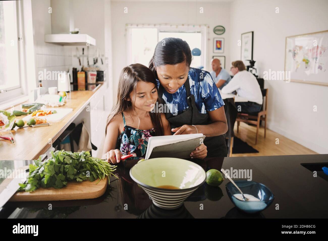 Mother and daughter reading recipe book while cooking in kitchen Stock ...