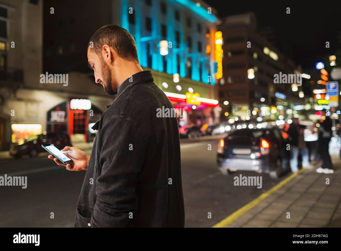 Side view of man using smart phone on city street at night Stock Photo ...