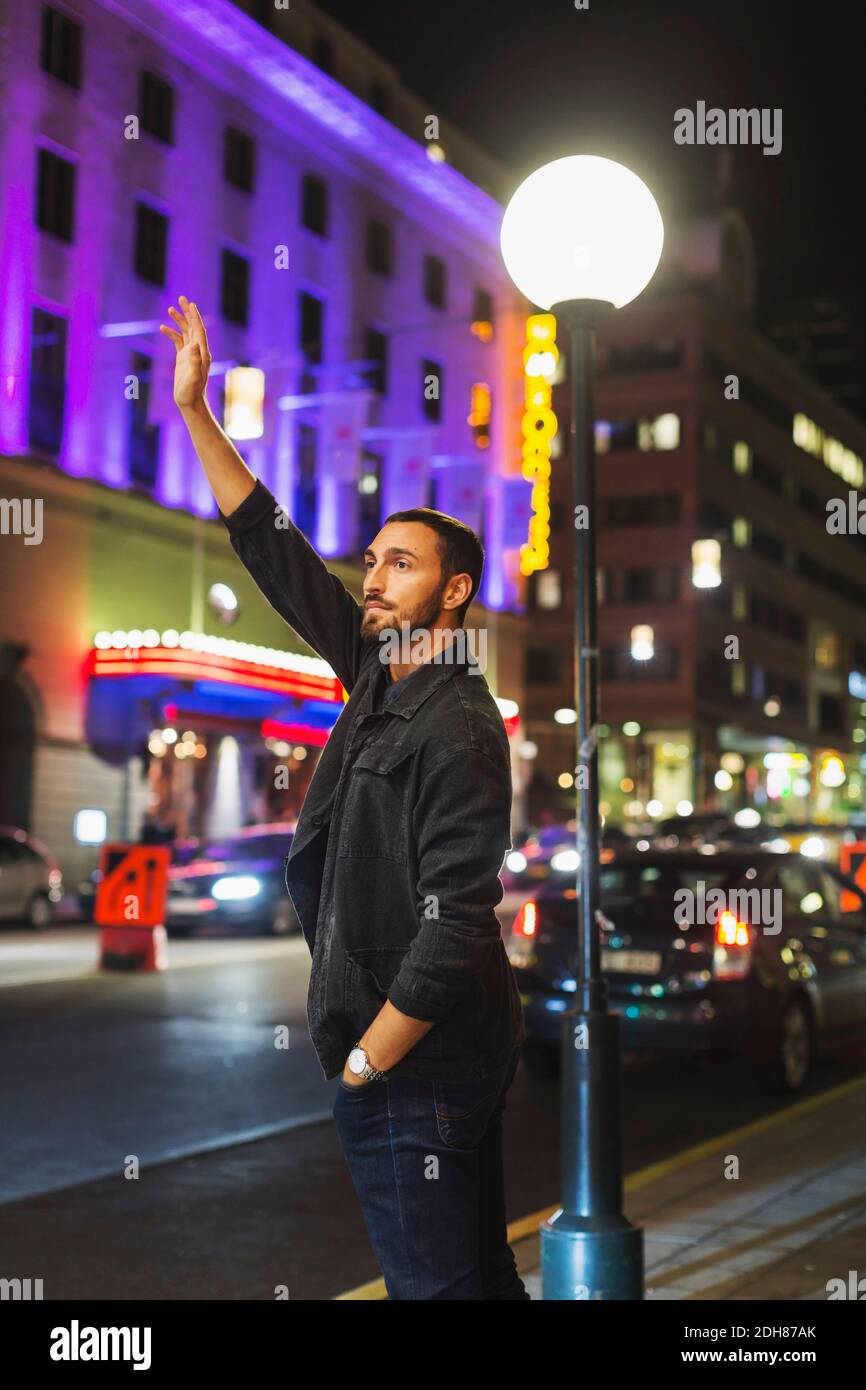 Side view of man hailing taxi on city street at night Stock Photo - Alamy