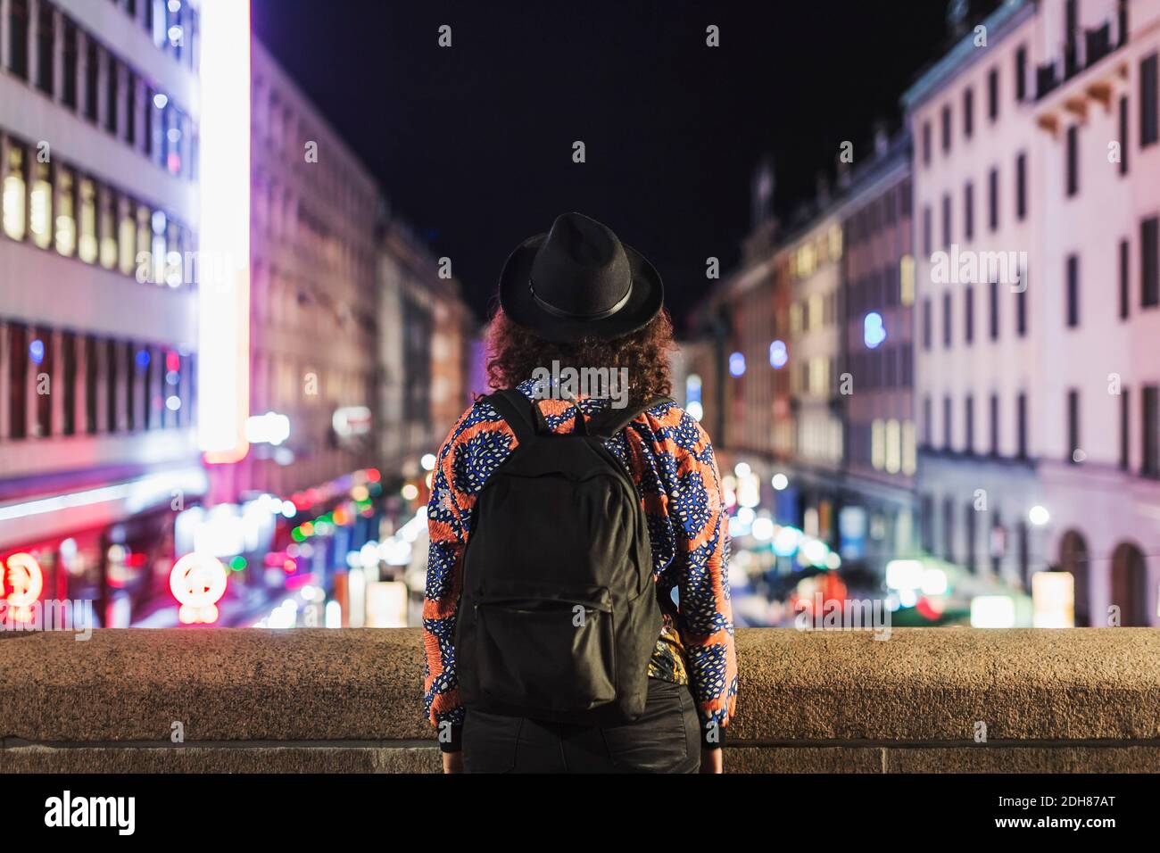 Rear view of woman carrying backpack standing on bridge in city at ...