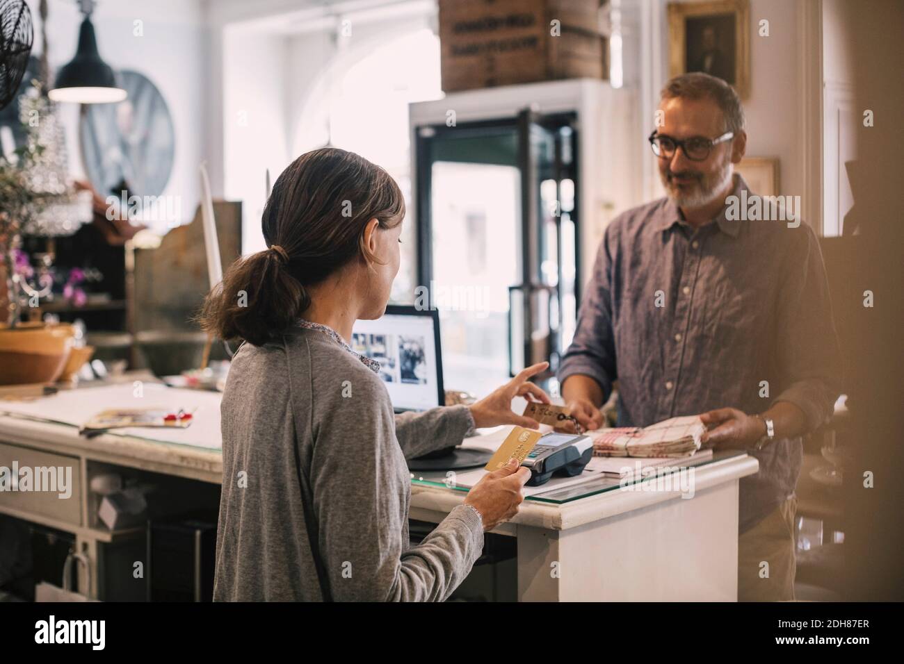 Female owner using credit card in front of customer standing at shop ...