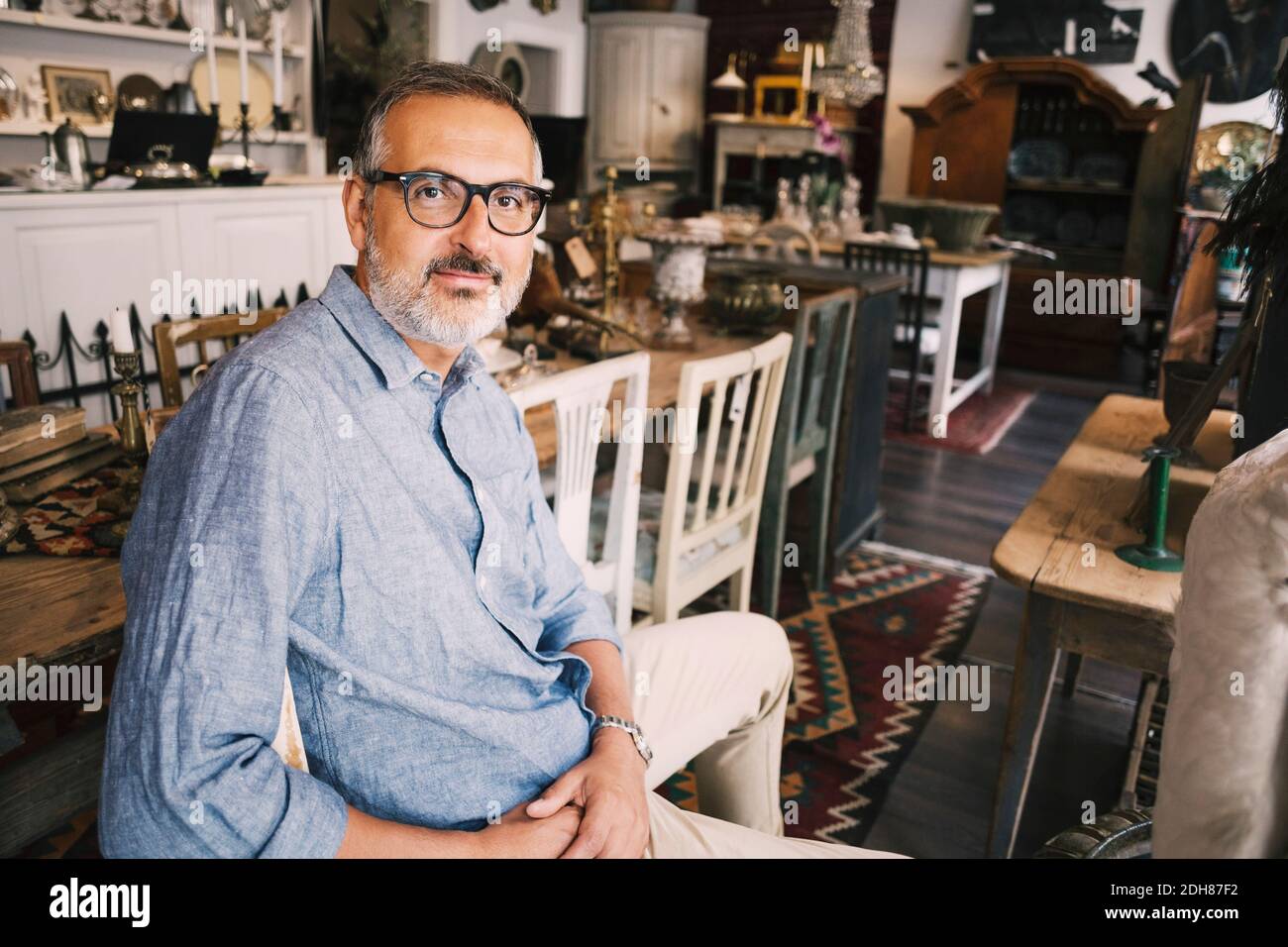 Portrait of confident owner sitting on chair at table in antique store ...