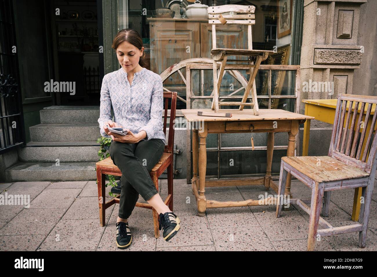 Woman using mobile phone while sitting on chair against store Stock ...