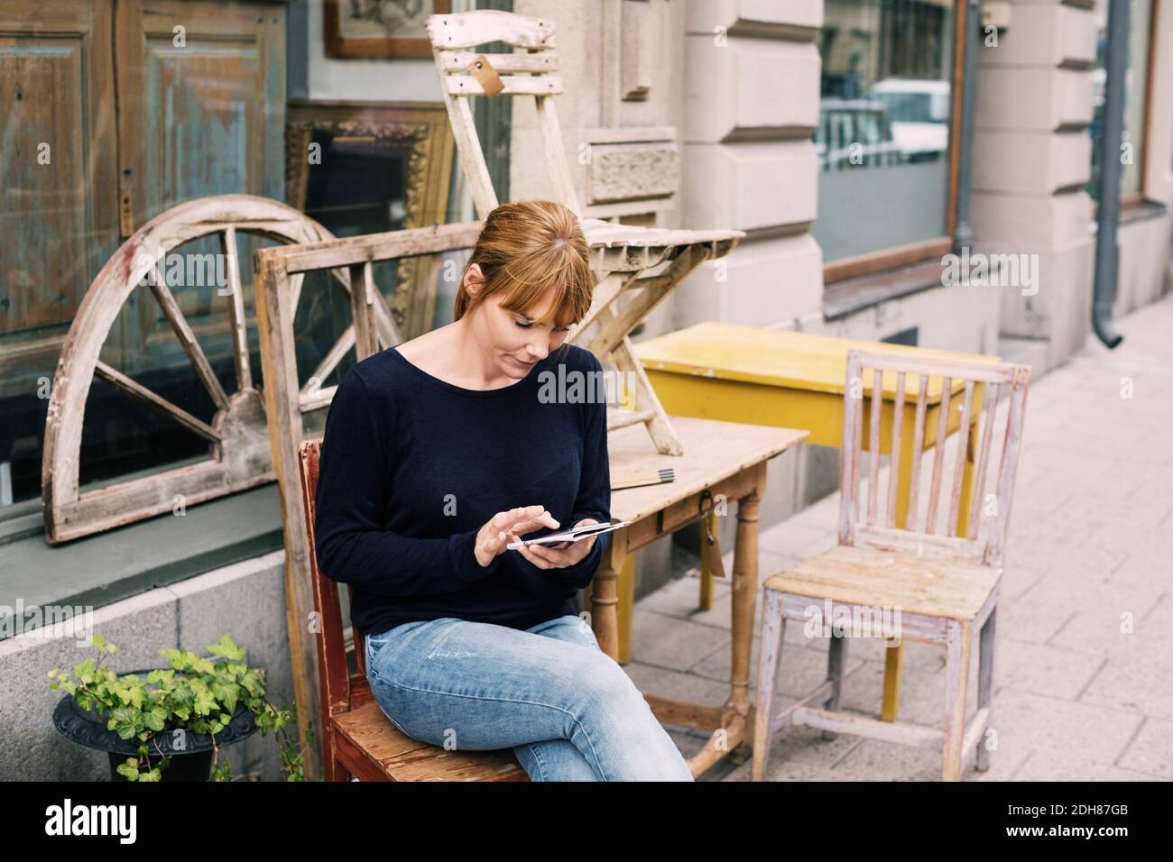 Woman using mobile phone while sitting on chair against store Stock ...