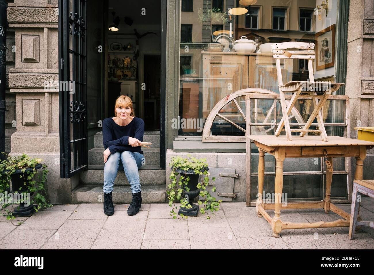 Female owner sitting on steps of antique shop Stock Photo - Alamy