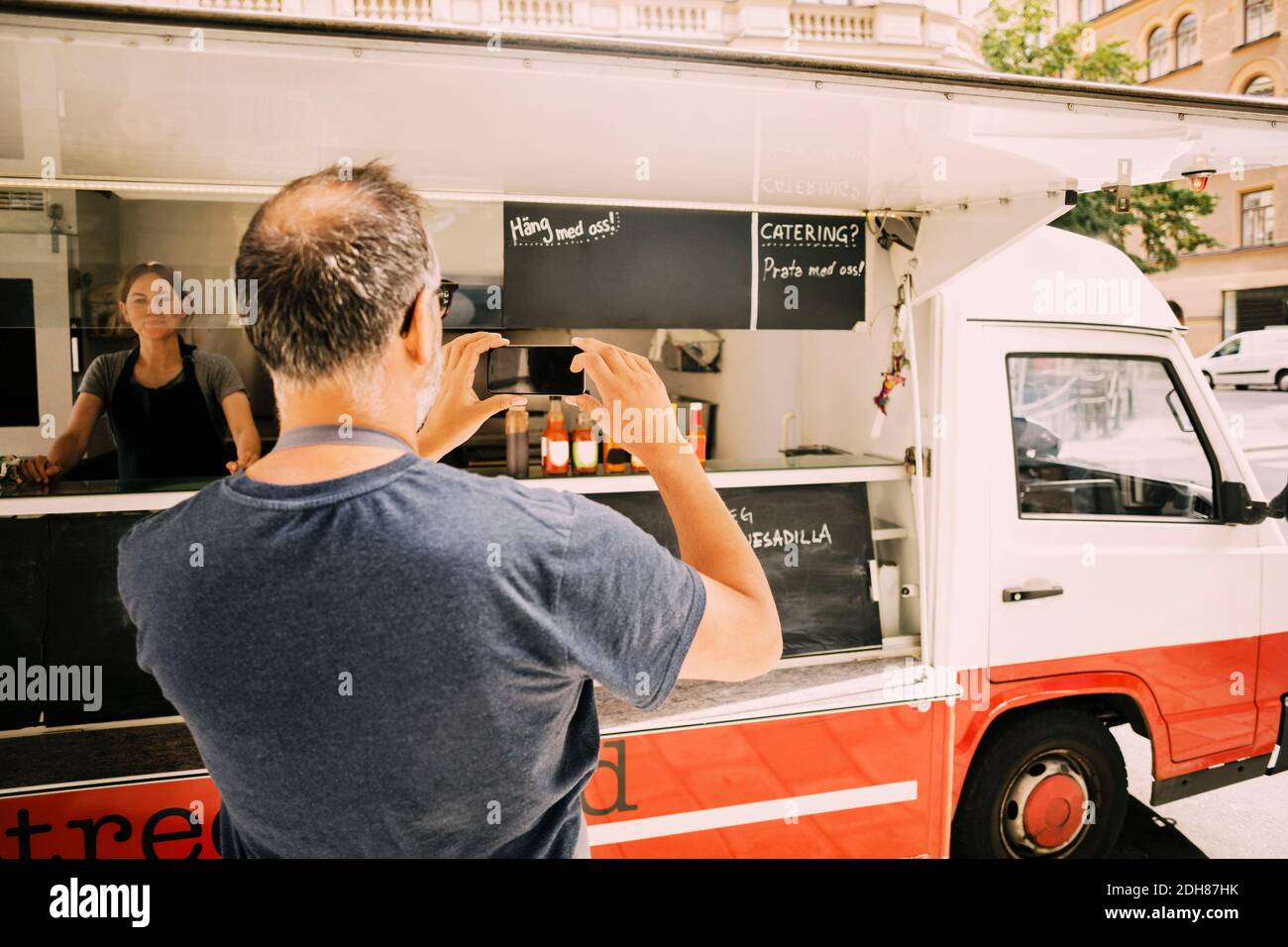 Rear view of owner photographing street food truck in mobile phone ...