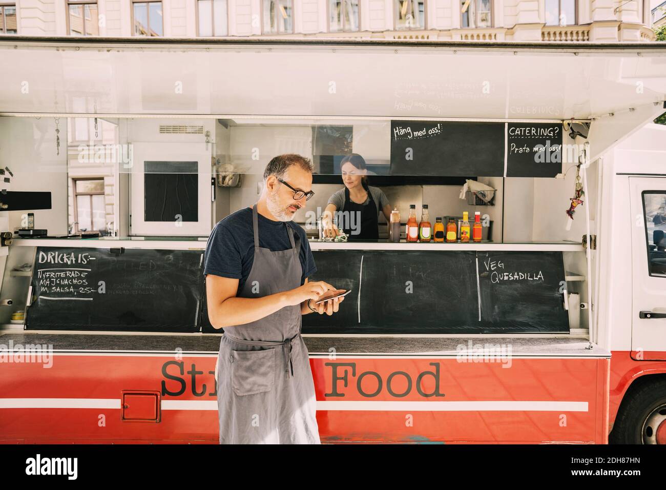 Mature chef using mobile phone against street food truck Stock Photo ...